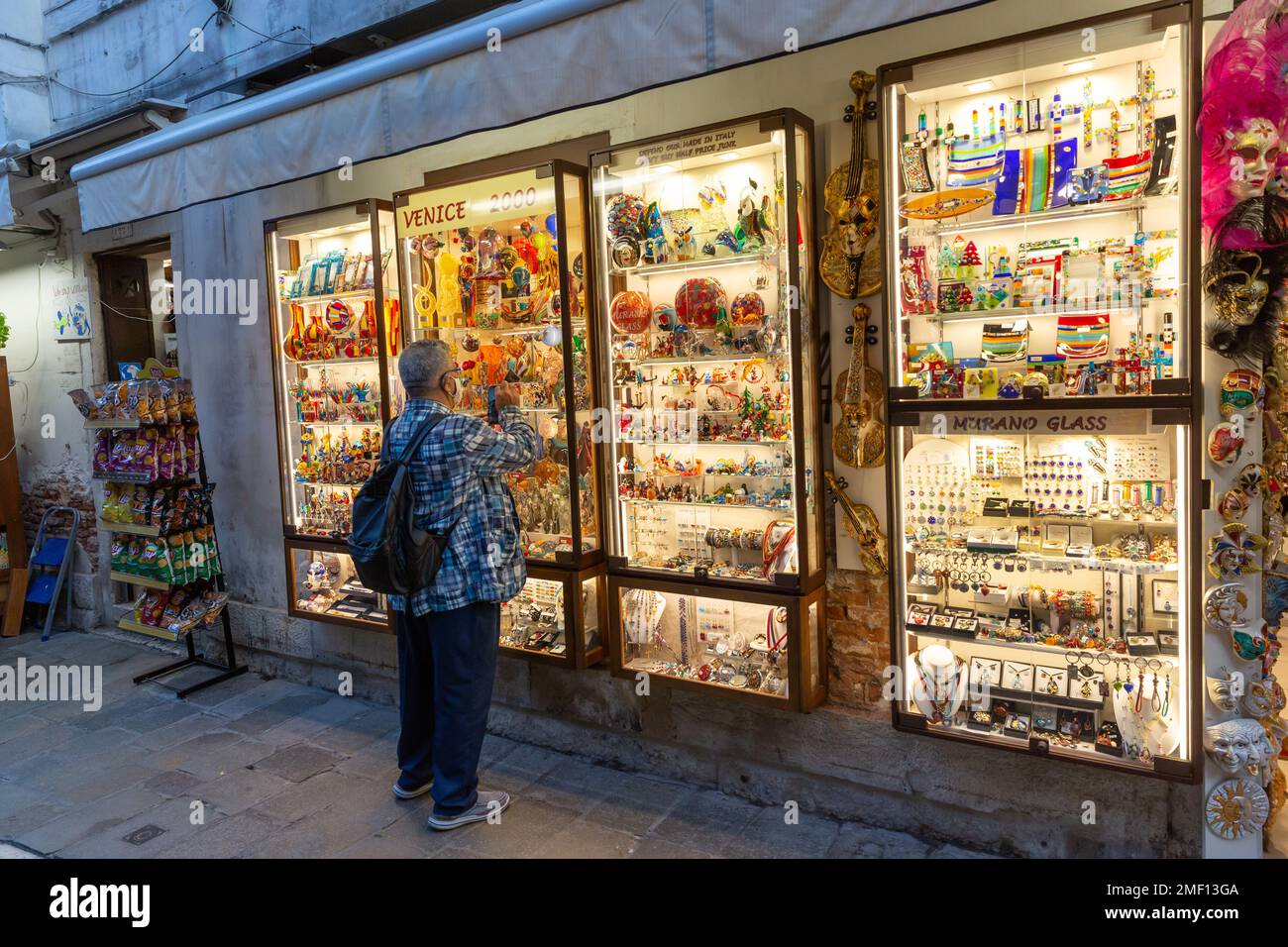 Face-masked tourist taking a photo of venetian glass souvenirs in shop window, Venice, Italy ...