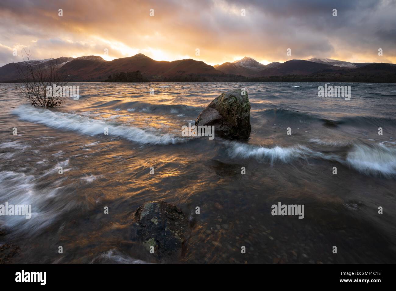Crashing waves on lake shoreline with dramatic sunset sky above ...