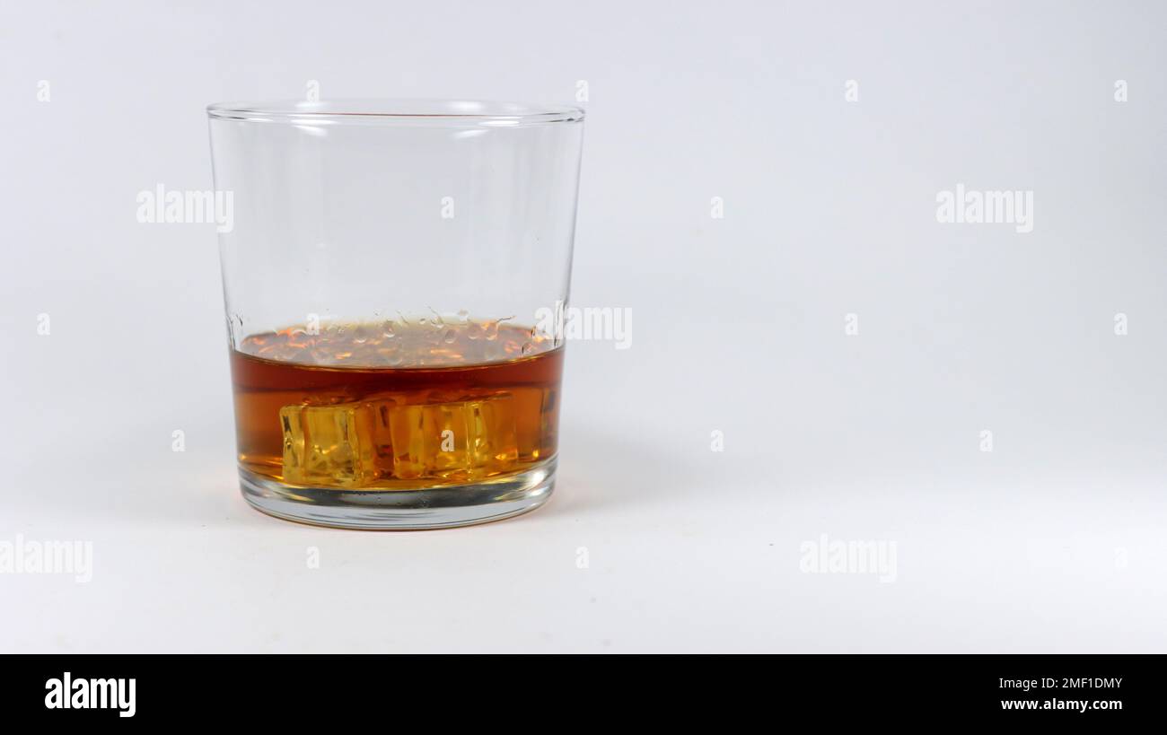 A glass with brown liquid and square ice cubes on a white background ...