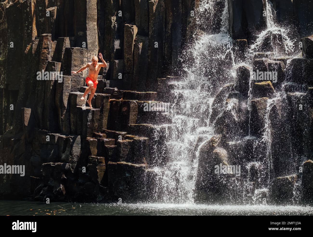 Middle-aged man jumping in waterfall lake. Falling water streams flow ...