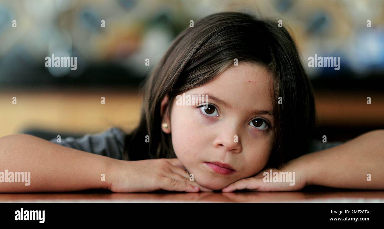 Cute small girl portrait face looking at camera child leaning on table ...