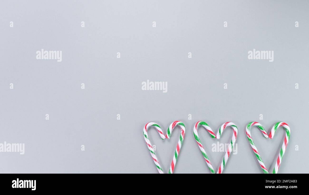 Red, green and white candy canes in the shape of heart on grey ...