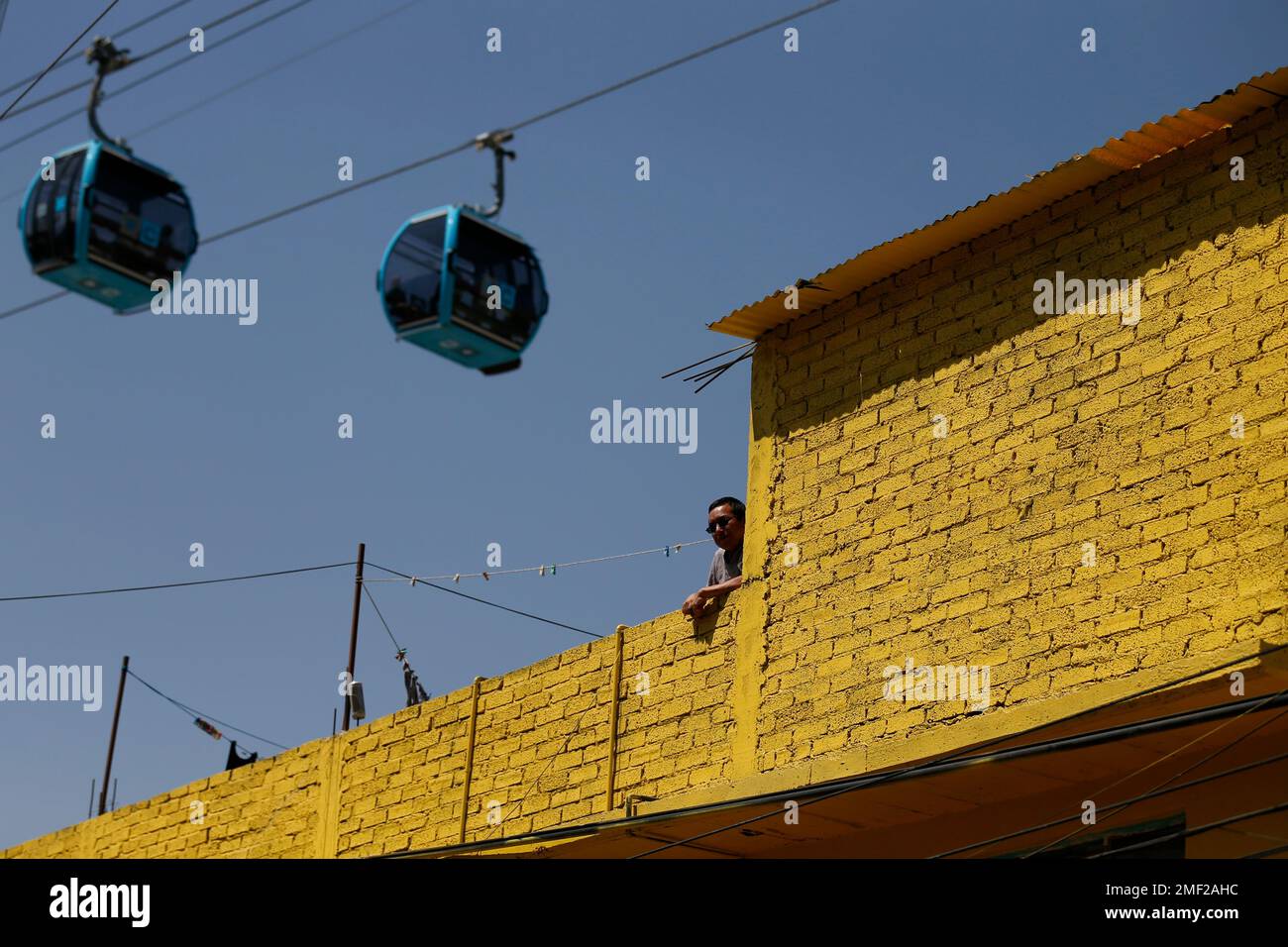 A man stands on a rooftop as cable cars overhead run between the Campos ...