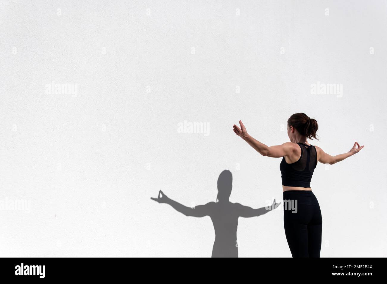 Sporty woman with arms raised creating a shadow against a white wall in ...
