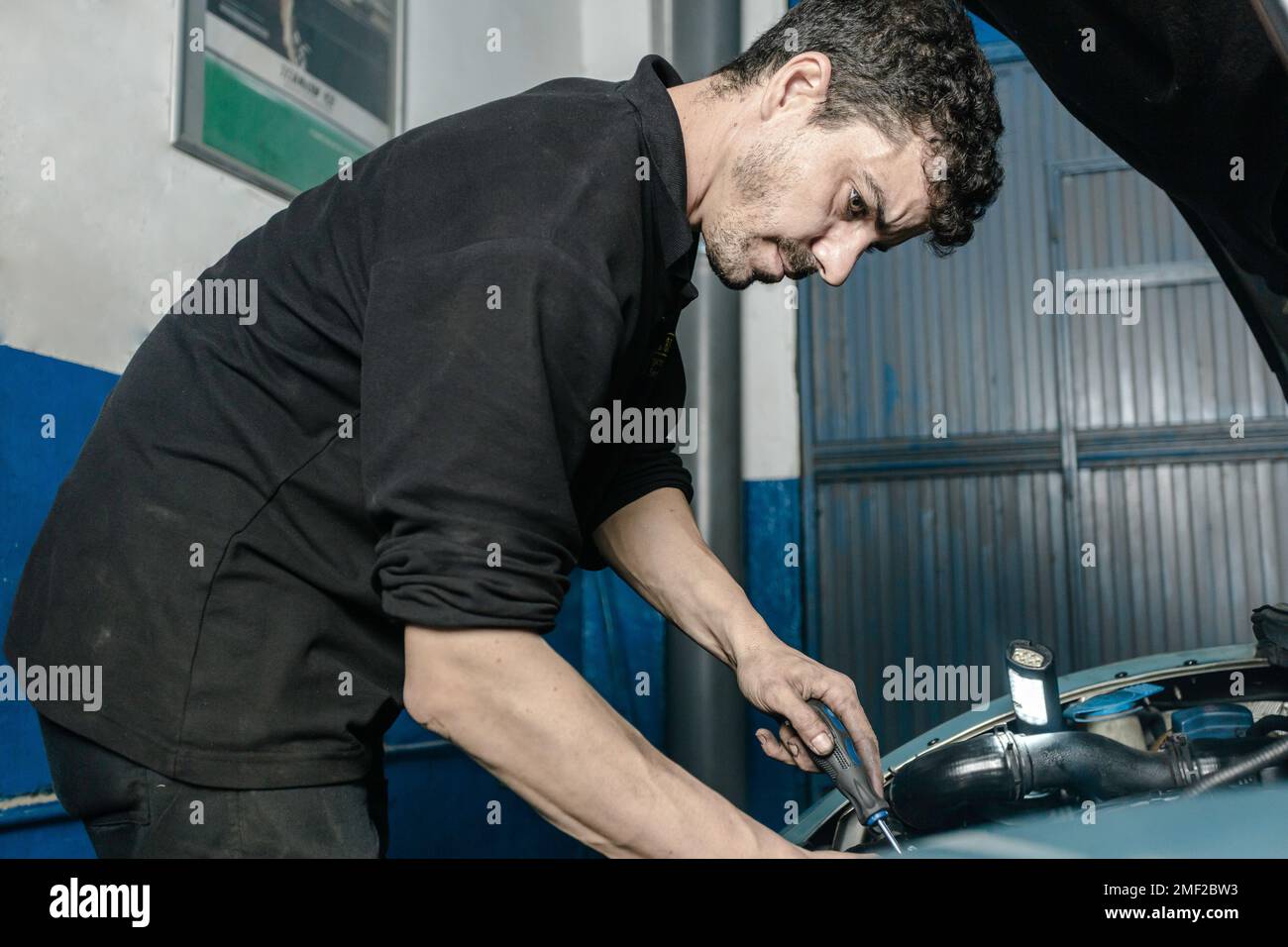 Mechanic using voltage tester screwdriver while checking battery of ...