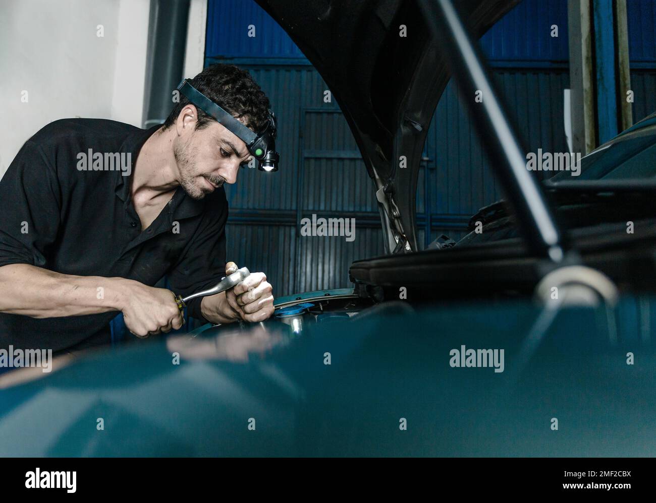 Side view of male technician with head flashlight using ratchet while ...