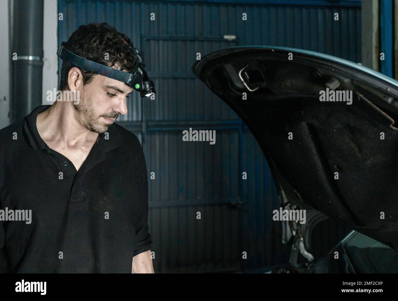 Side view of male technician with headlamp at auto service station ...