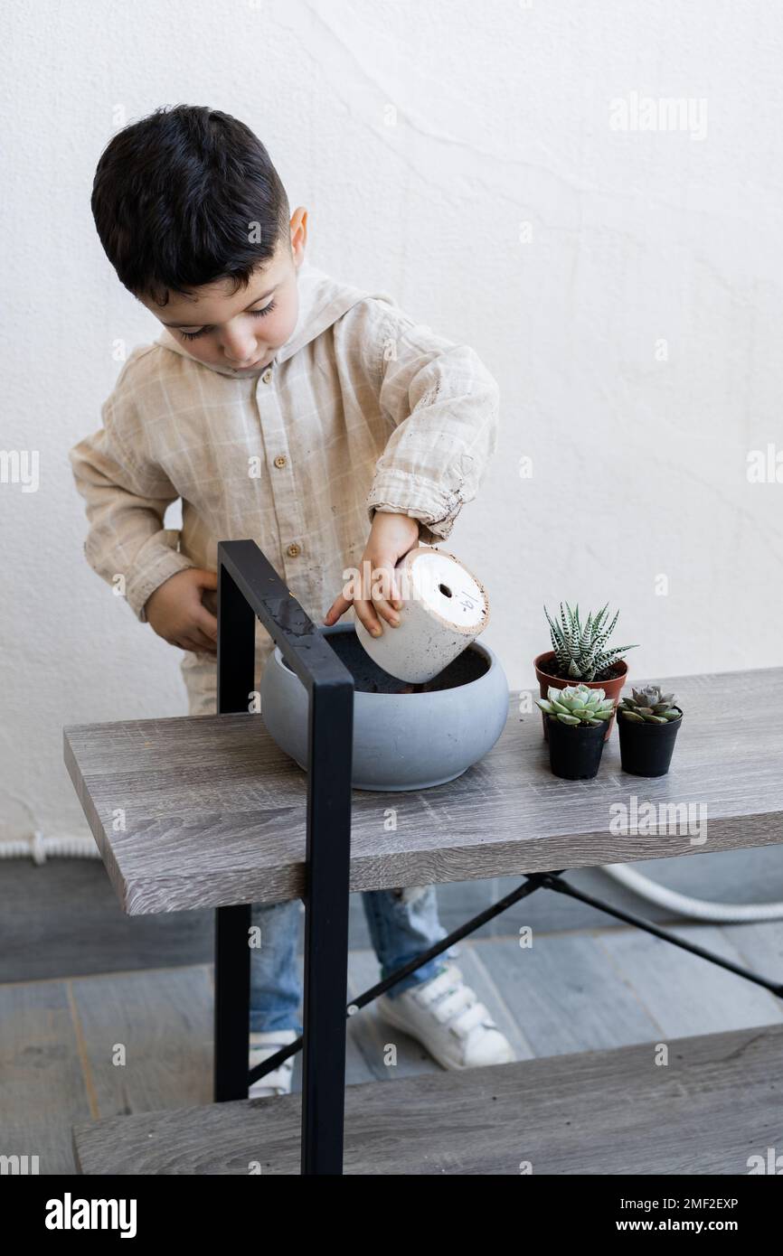 Funny boy planting on the balcony. Little child shovels ground, putting ...