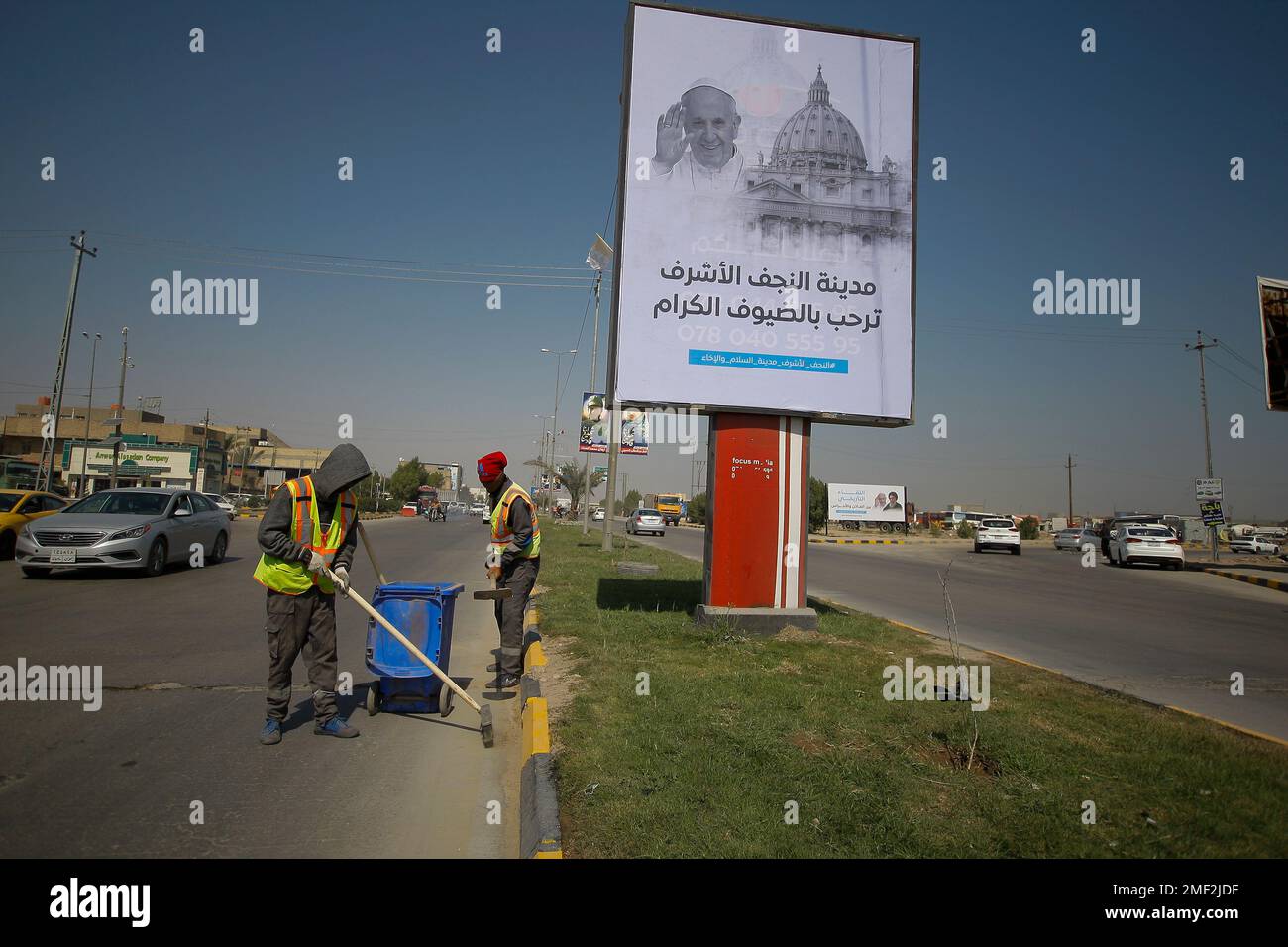 Iraqis clean street by a poster announcing the upcoming visit of the ...