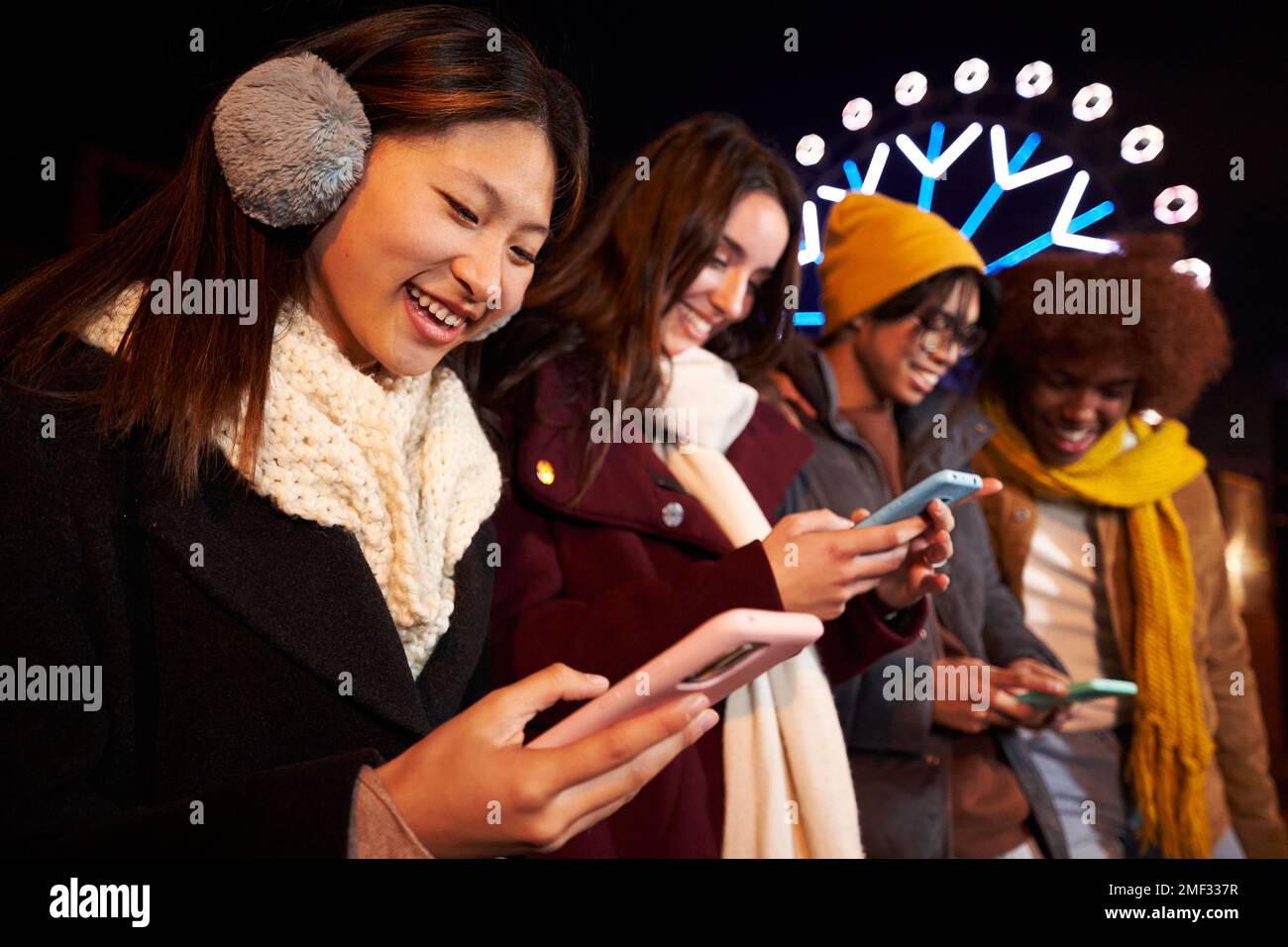 Side view of a group of friends using their cell phones at an amusement ...