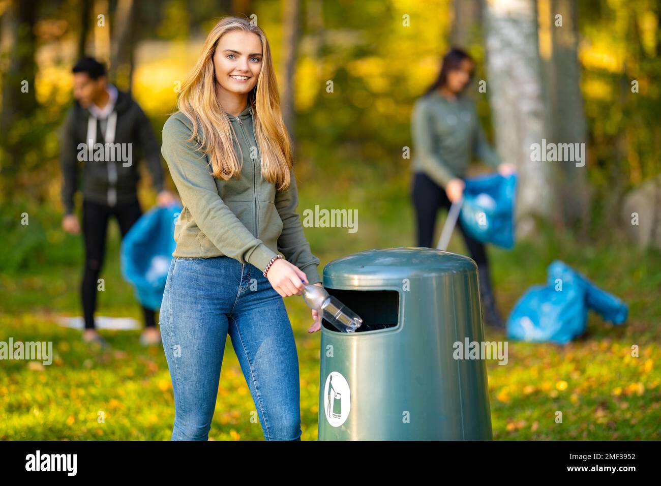 Smiling young woman putting bottle in garbage bin Stock Photo - Alamy