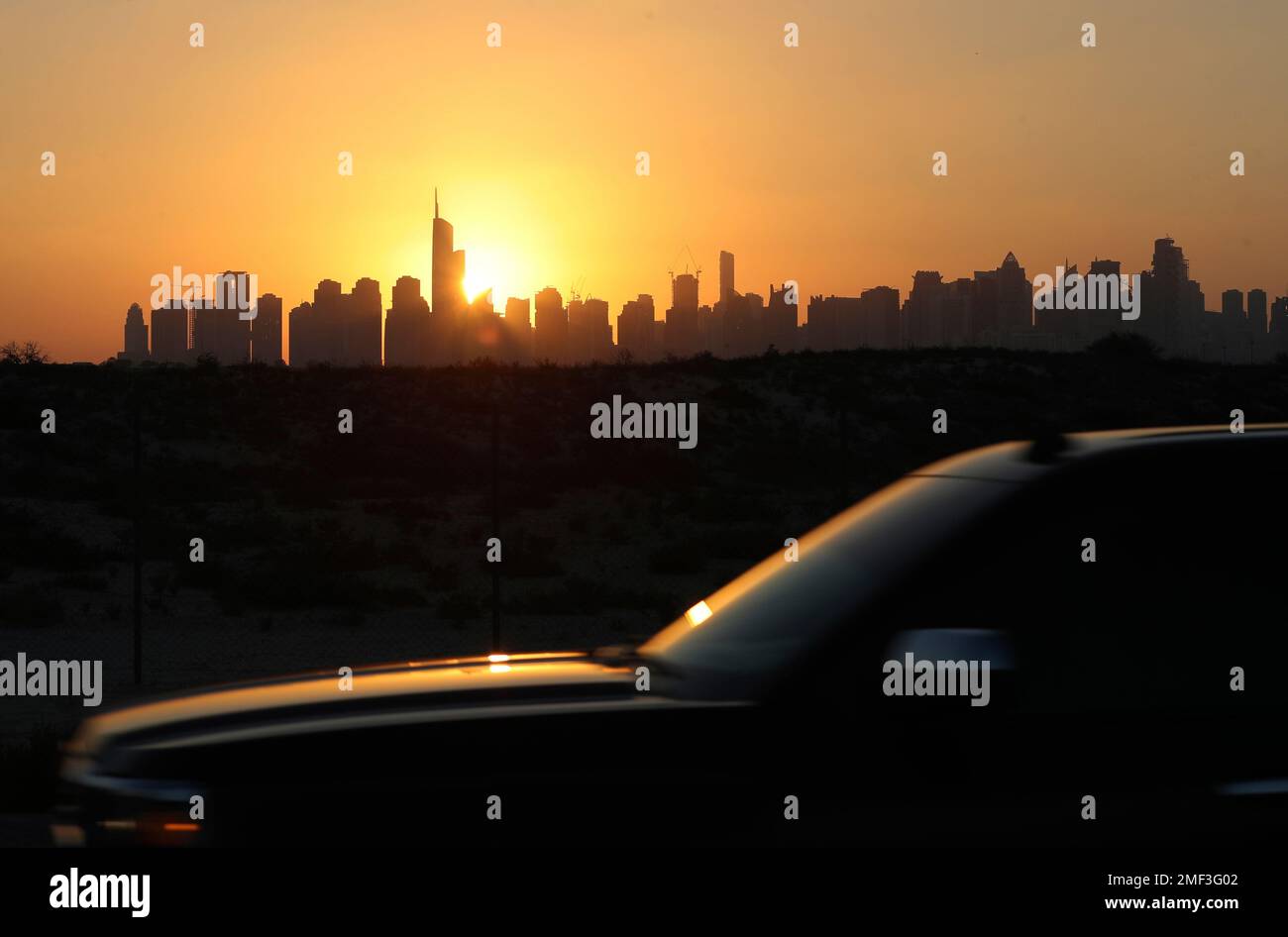 The sunlight reflects on a car glass as it sets behind the city skyline ...