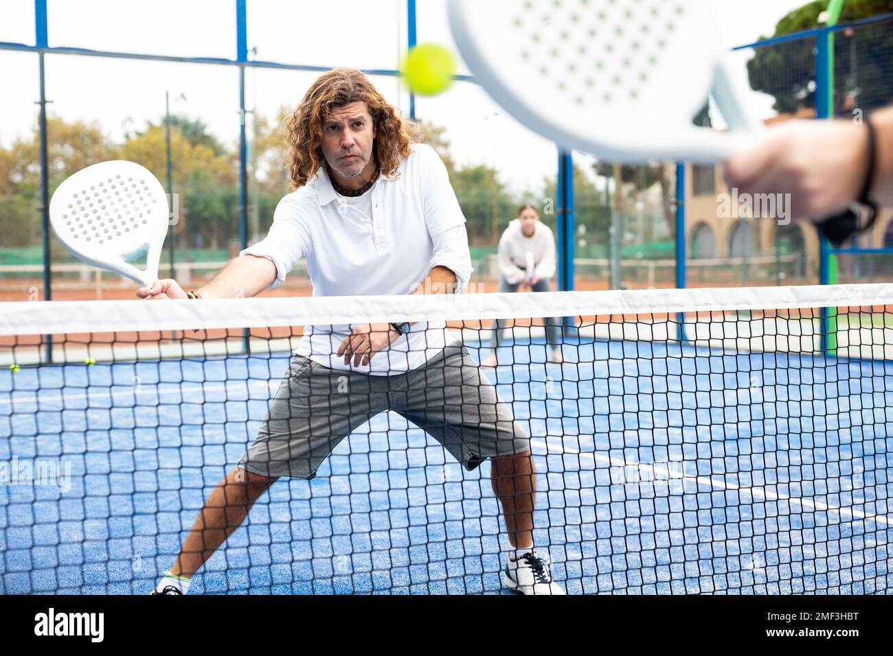 Focused middle-aged Latin man padel player hitting ball with racket on ...