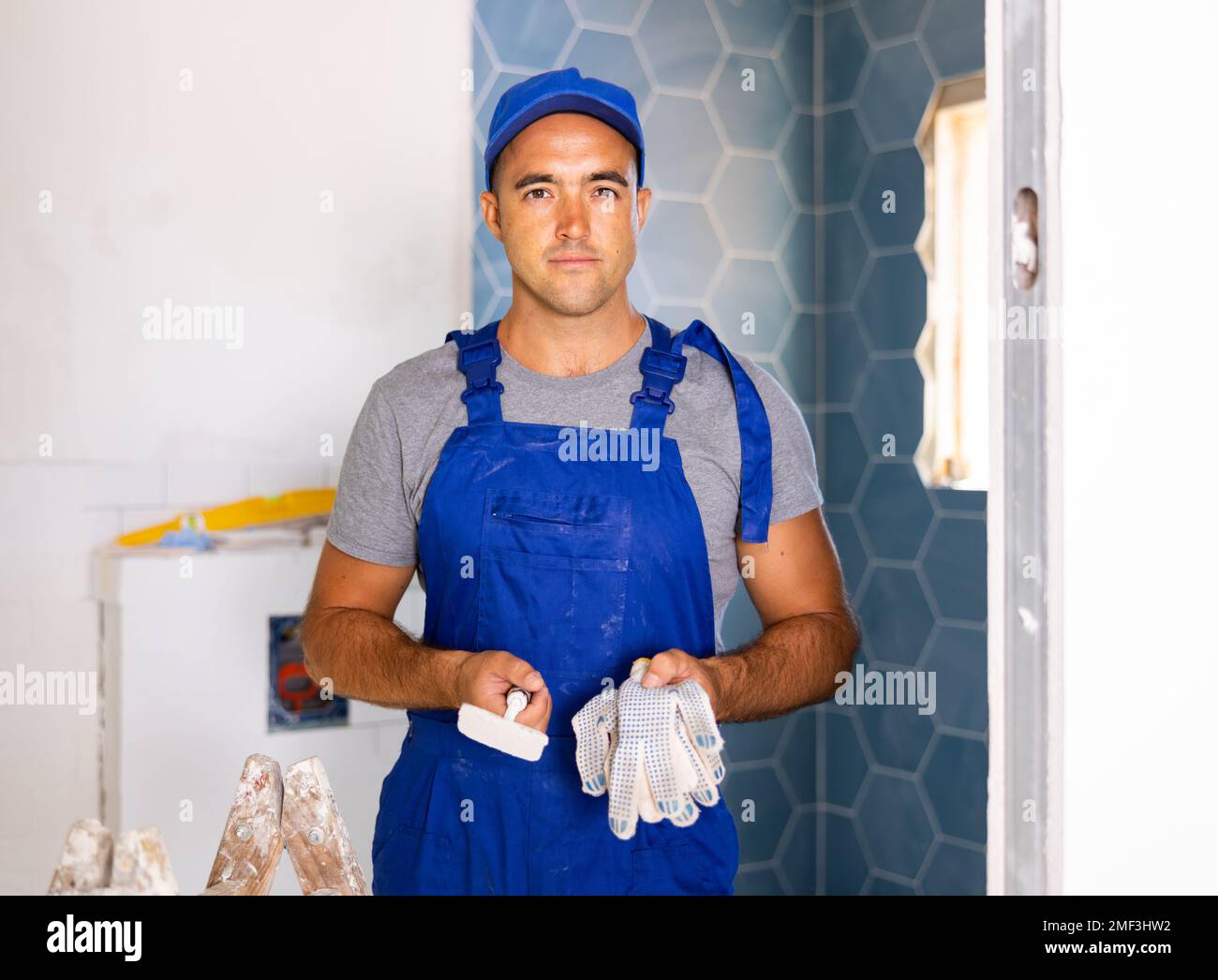 Professional man builder in blue construction overalls and cap posing ...