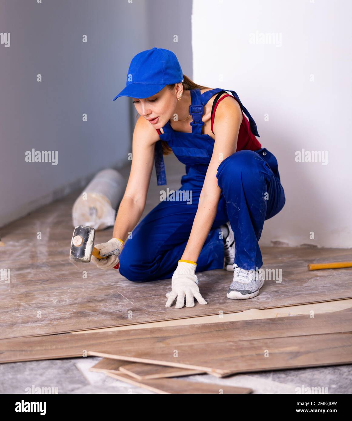 Concentrated woman in blue construction overalls laying laminate ...