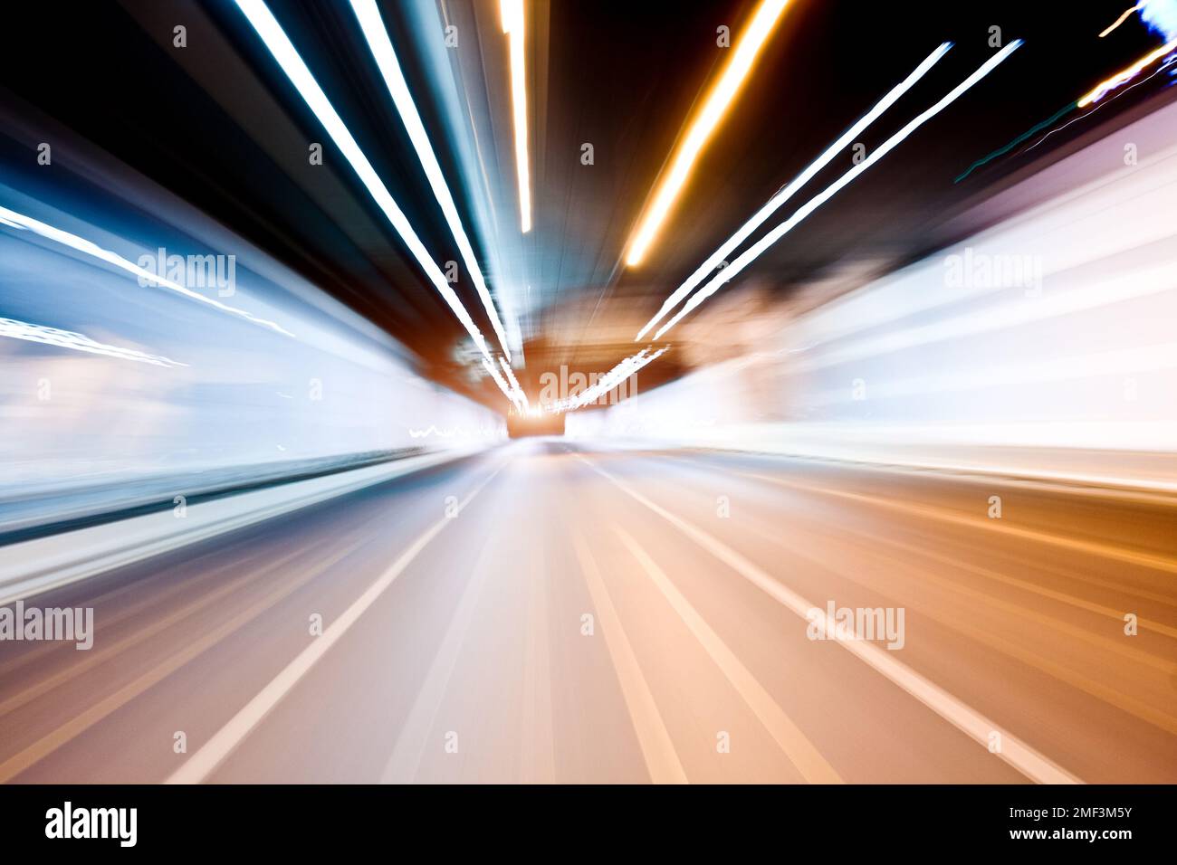 A motion blur shot of an empty road under a tunnel with white lights ...