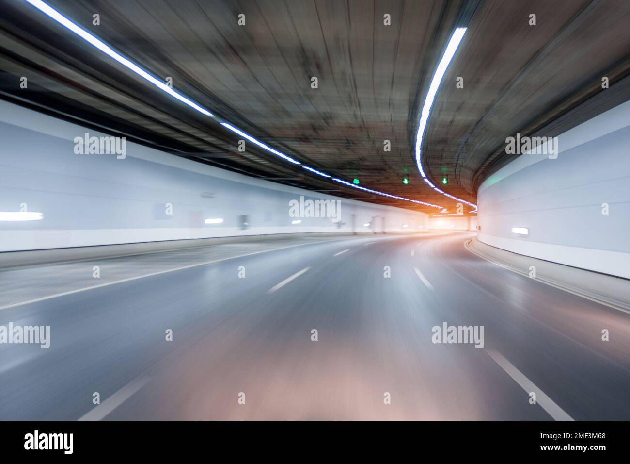A motion blur shot of an empty road under a tunnel with white lights ...