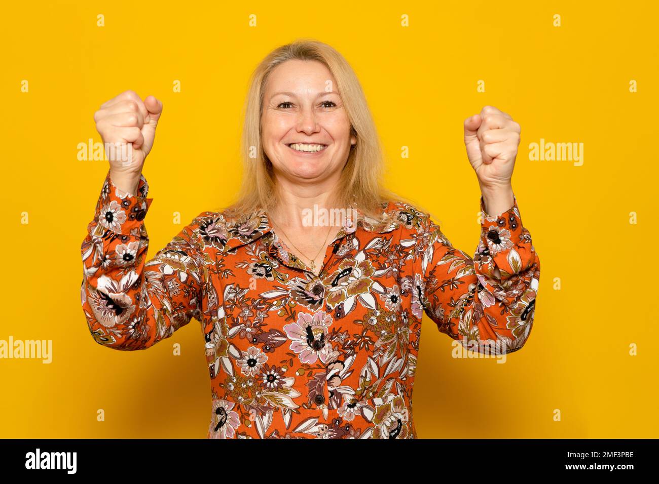 Happy caucasian successful woman in a patterned dress with raised hands ...