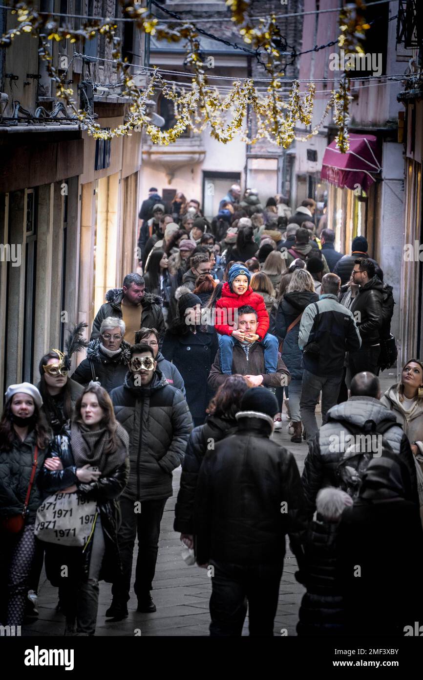 A man walks at the street in the dark grey crowd with his son in red ...