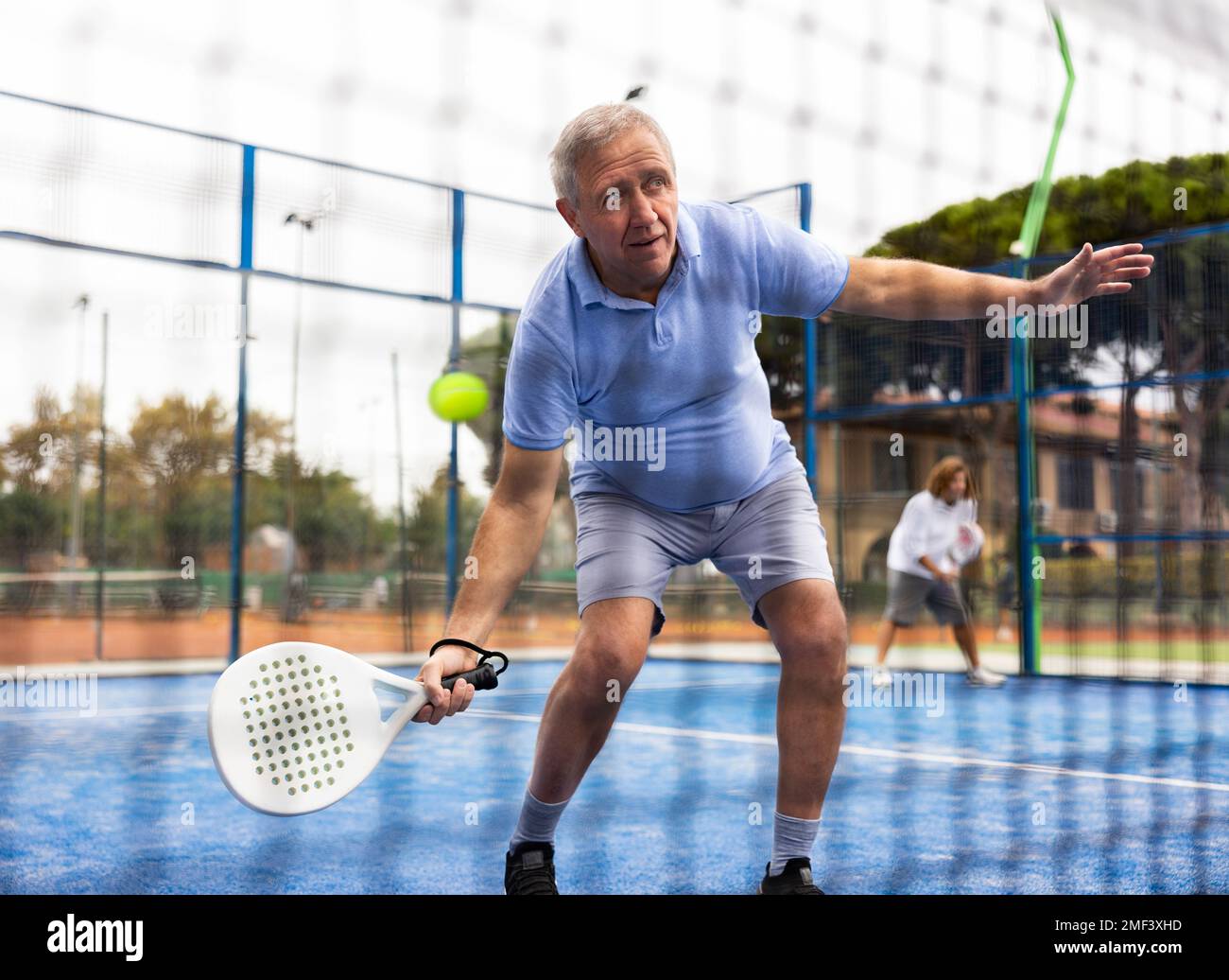 Positive elderly male player serving ball during training padel in ...