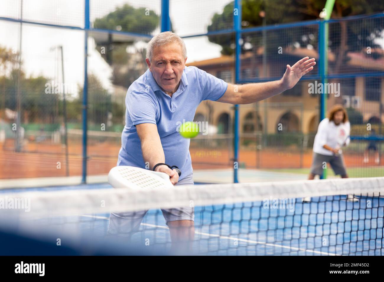 European old man holding padel racquet in hand and ready to return ball ...