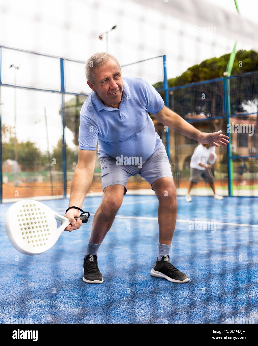Concentrated elderly woman padel player hitting ball with a racket on ...