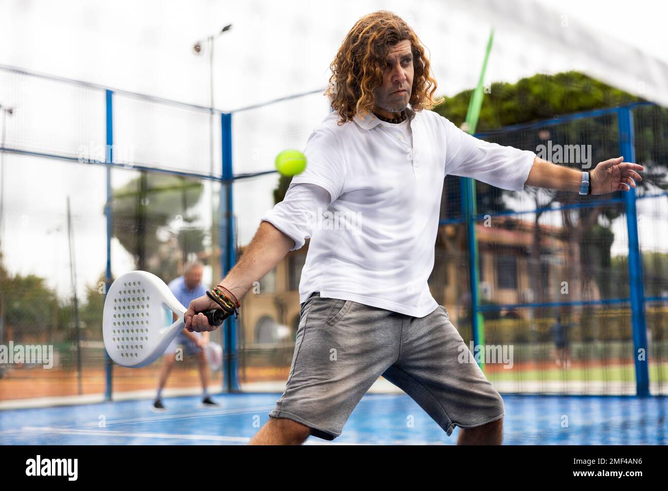 Focused middle-aged Latin man playing padel on court. View through ...