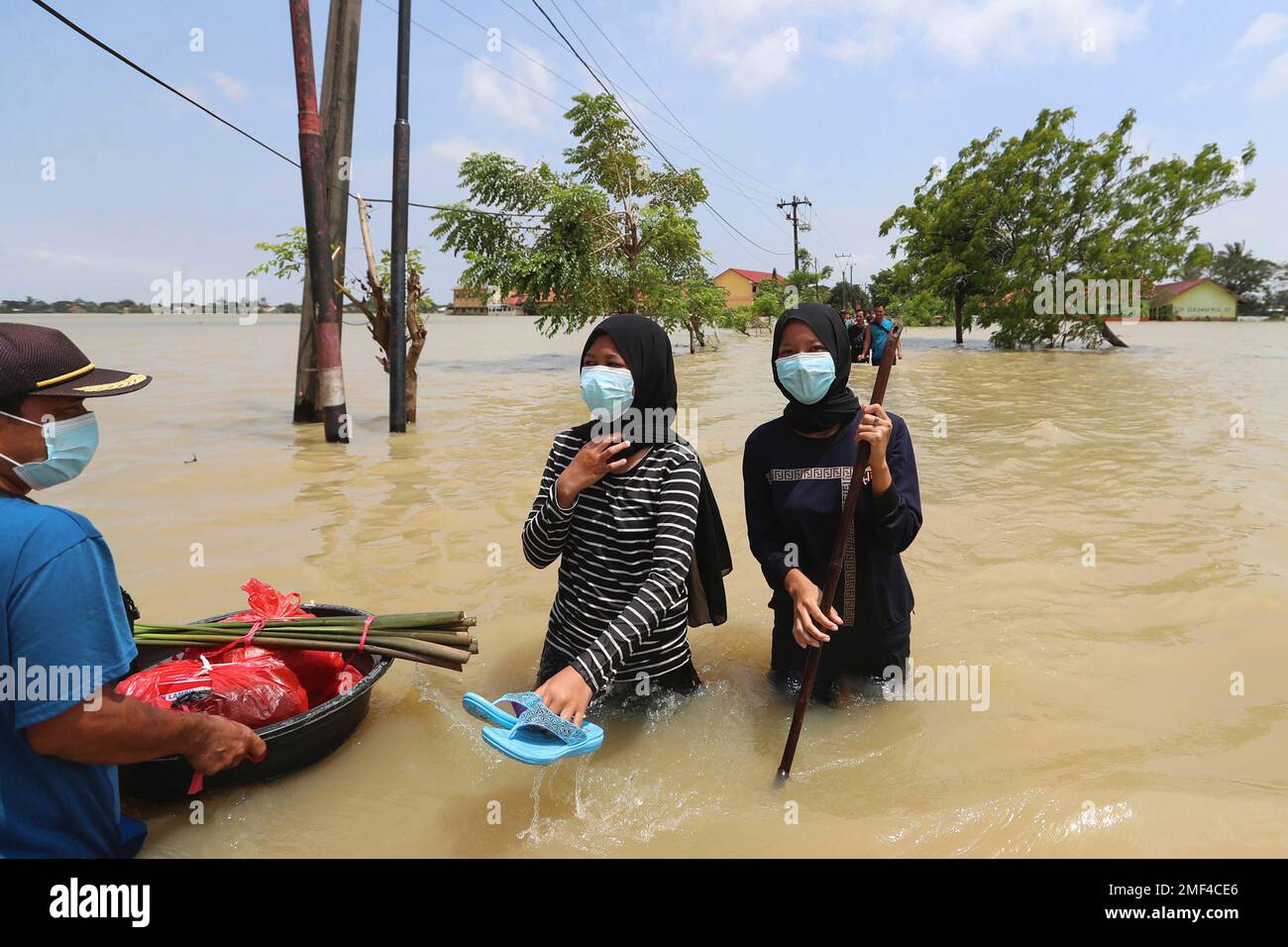 Indonesians carry their belongings as they wade through the water in a ...