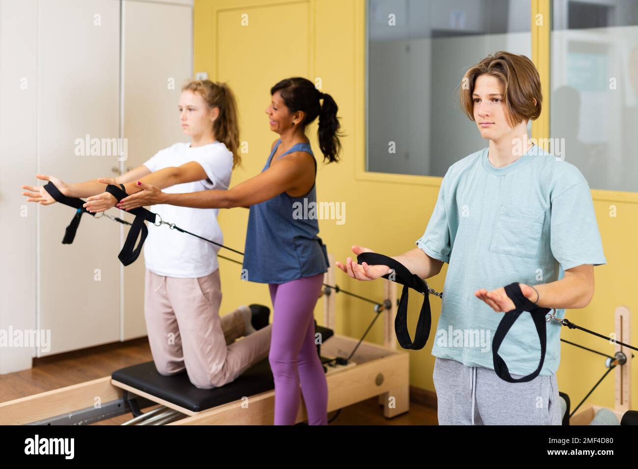 Pilates instructor helping teen boy and girl doing exercises on ...