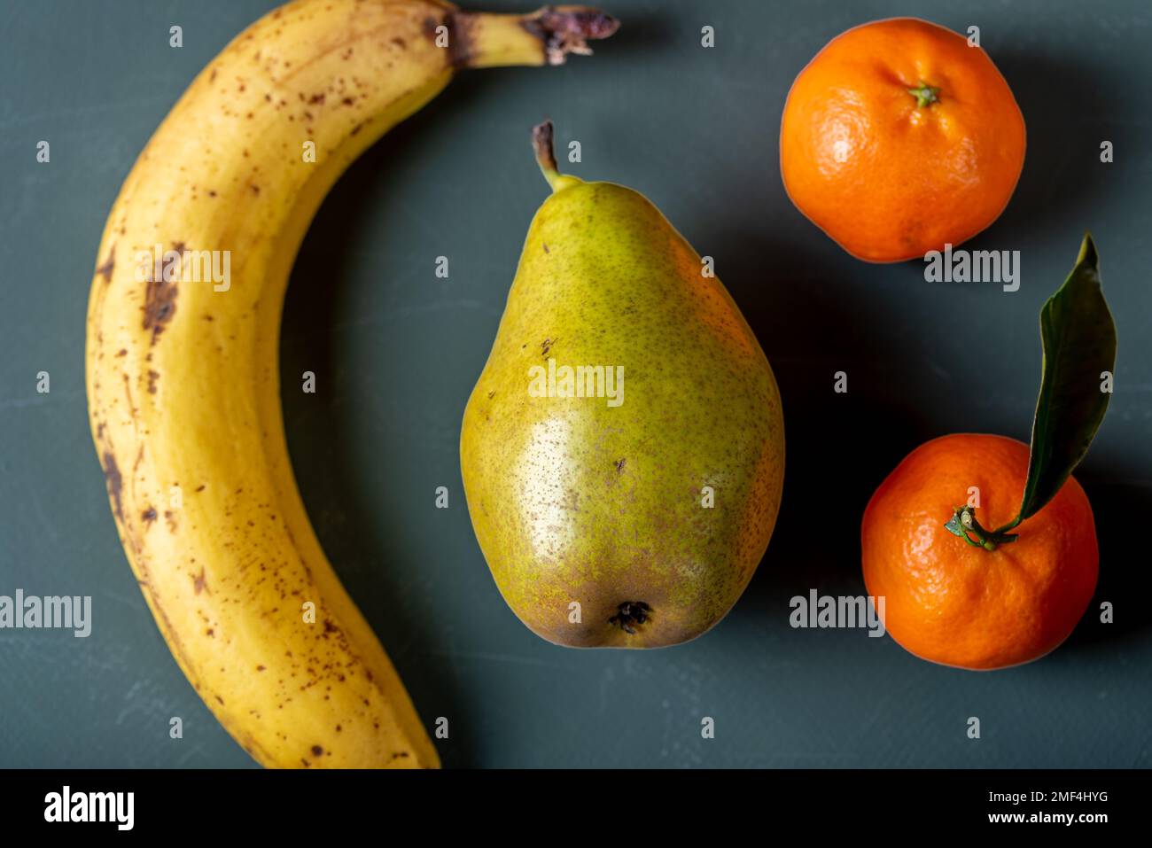 Fruits on green background. One banana, one pear and two mandarins on ...