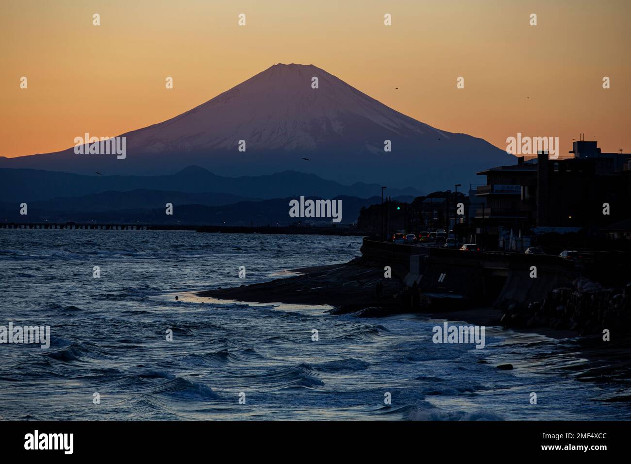 Silhouetted against the sunset colored sky Mount Fuji is viewed from a ...