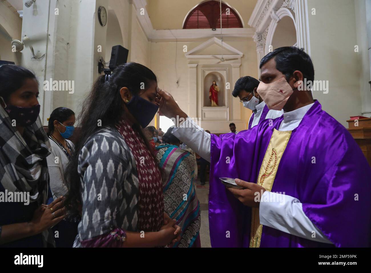 A Catholic priest marks the forehead of a devotee with the symbol of a ...