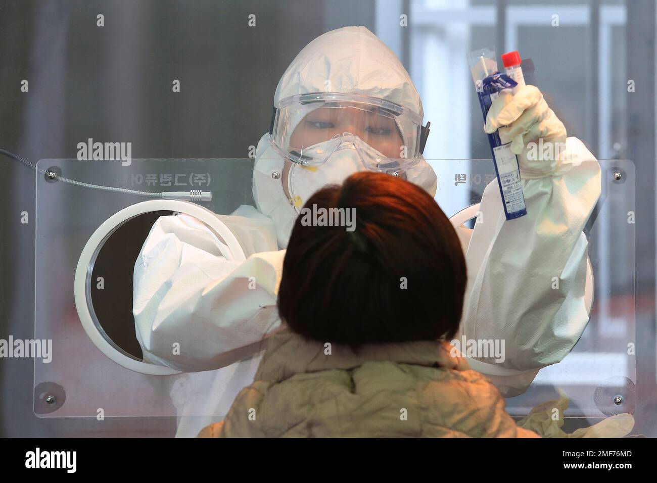 A medical worker in a booth takes a nasal sample from a woman at a ...