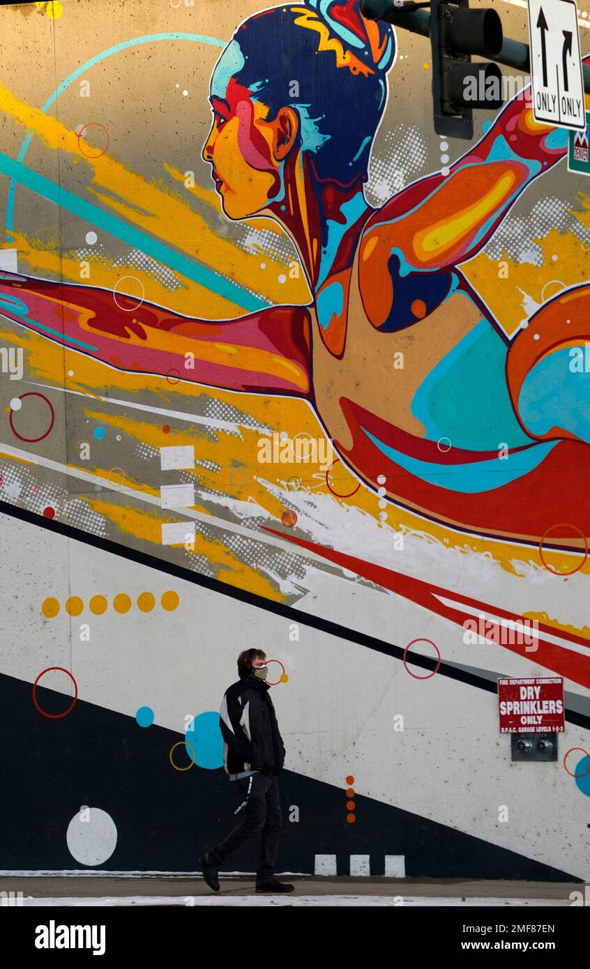 A lone pedestrian in a face covering passes by a mural on a wall at the ...