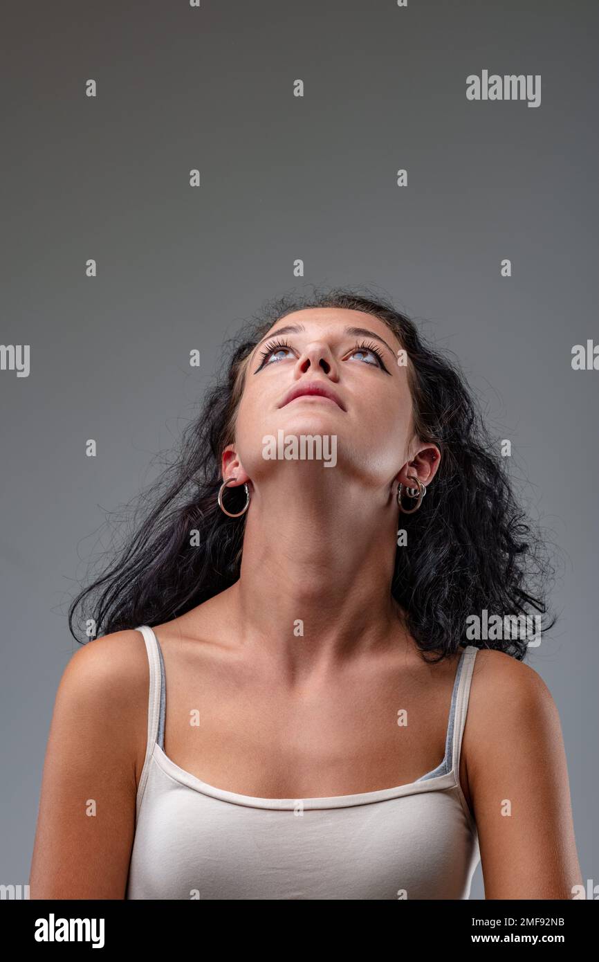 Frontal portrait of a young brunette girl in a tank top looking up by ...