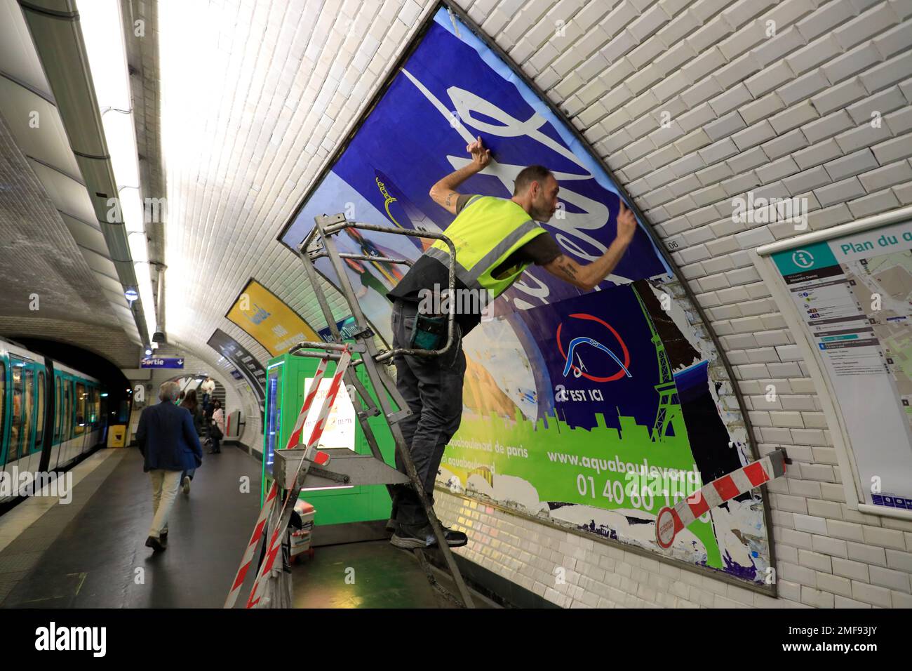 A worker putting up commercial advertising poster on the wall inside of ...