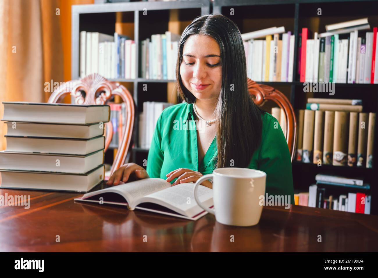 Young woman reading book in her personal library with bookshelf behind ...