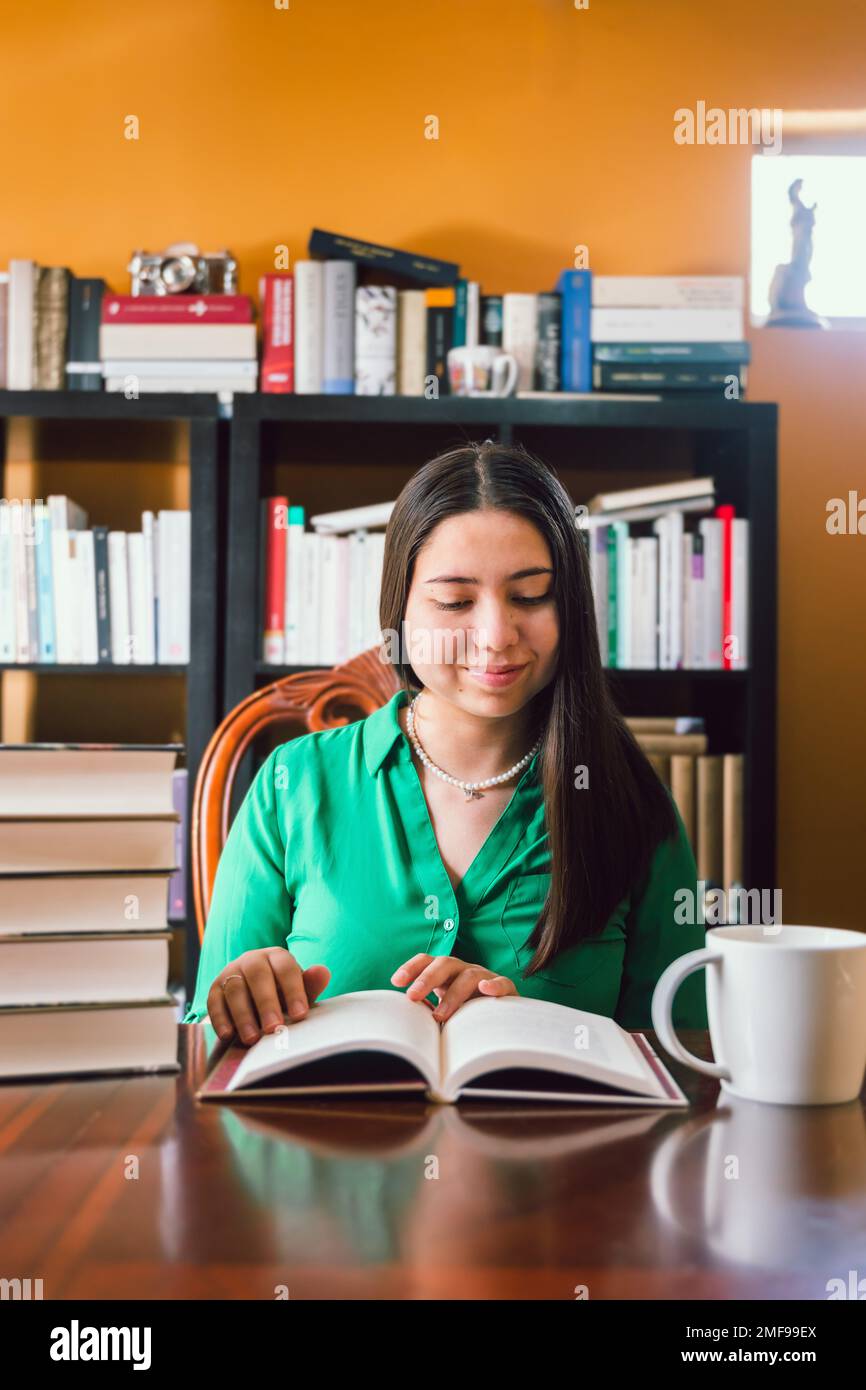 Young woman reading book in her personal library with bookshelf behind ...