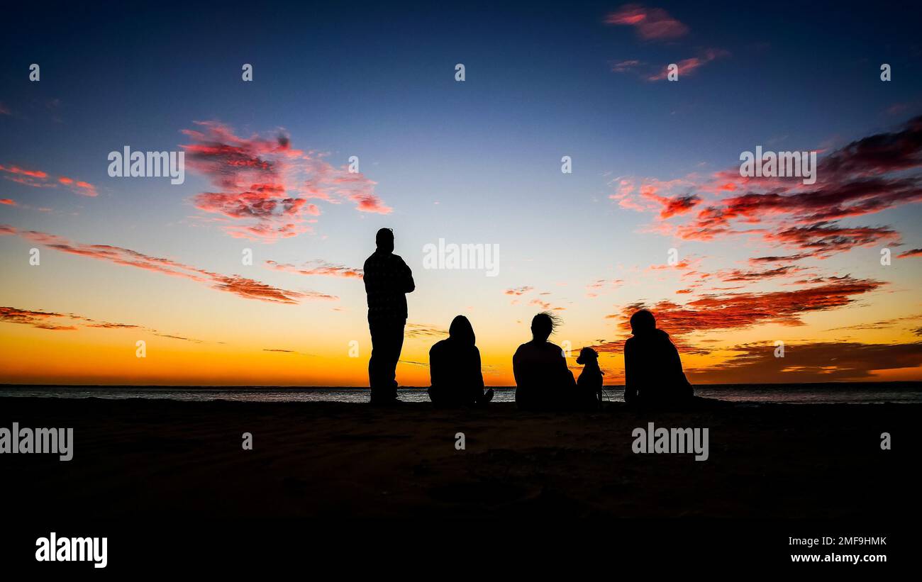 A silhouette of people watching vibrant sunset from the seashore Stock ...