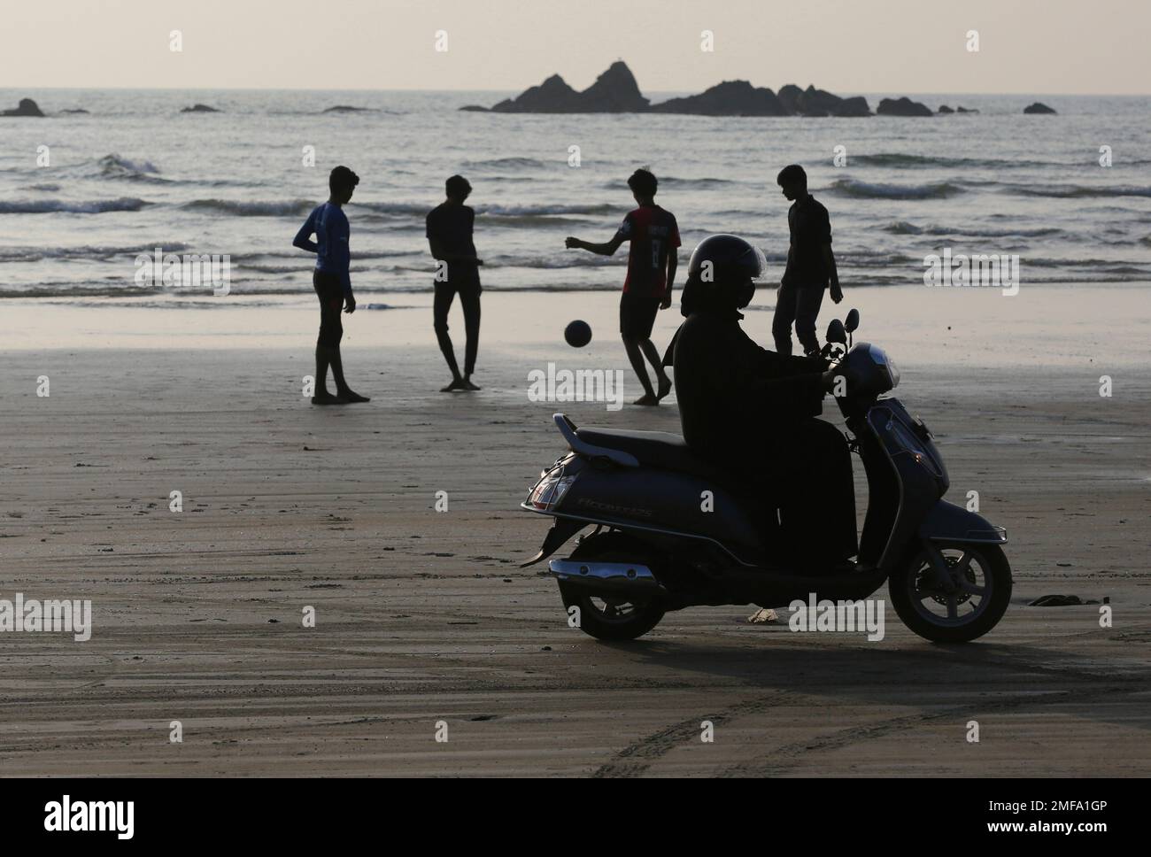 A woman rides past boys playing a game of beach football at ...