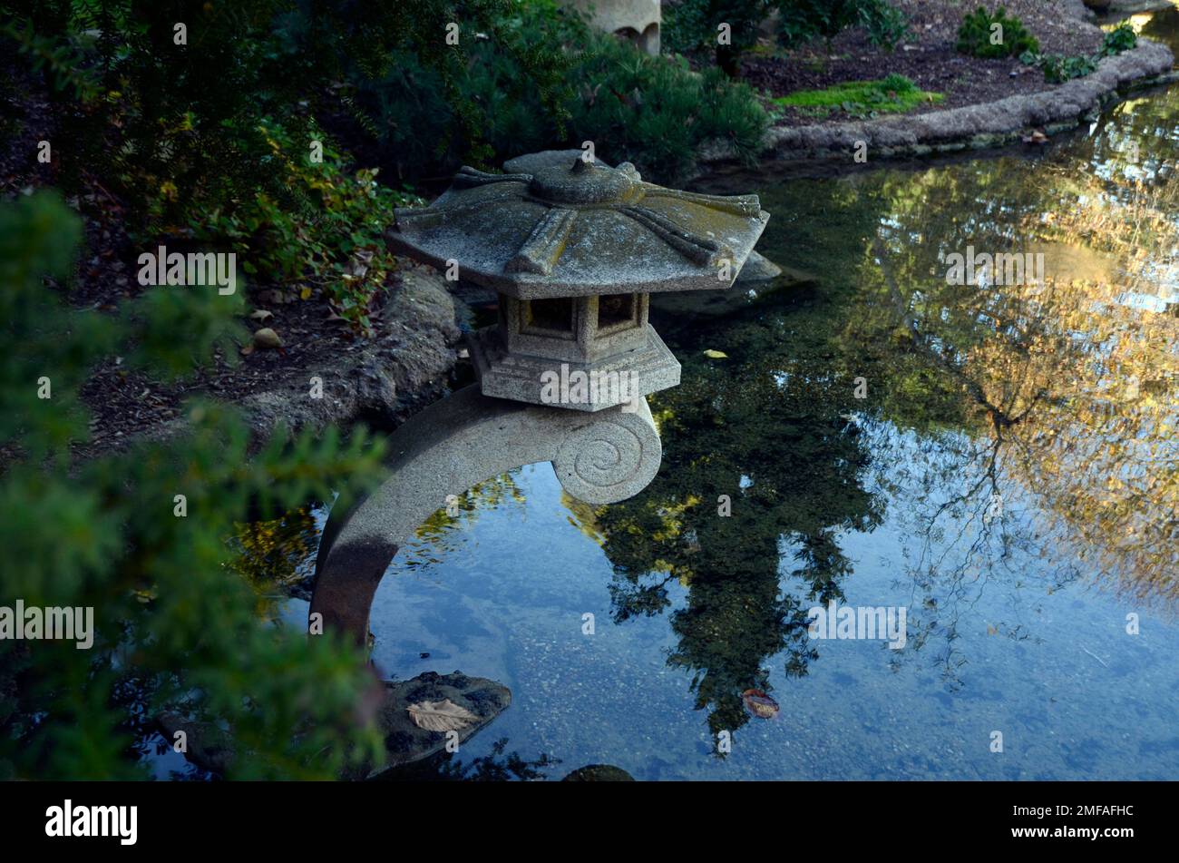 A vintage stone lantern hangs over a reflecting pond with images of ...