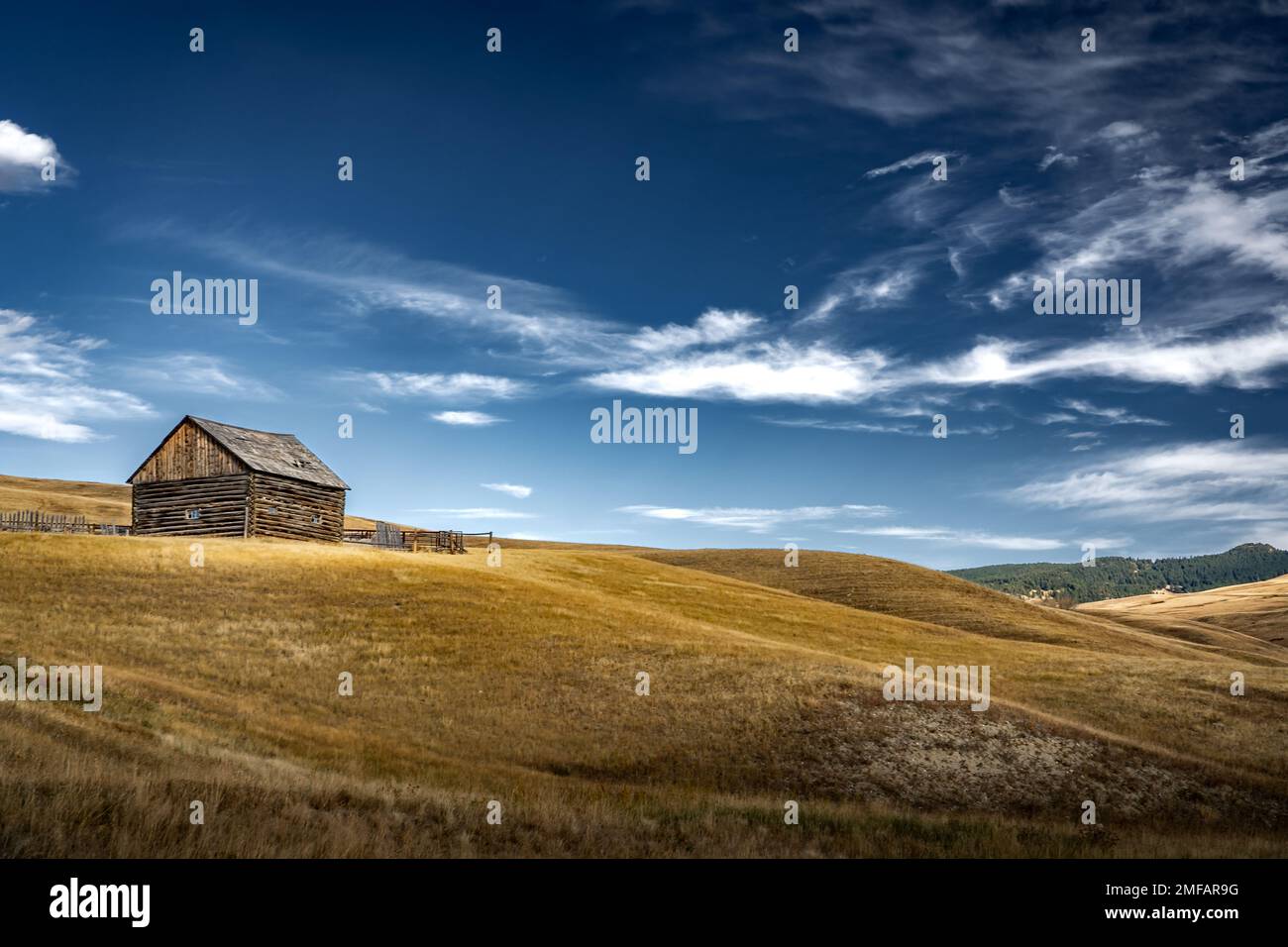 A small log cabin on a hillside under a deep blue sky along the Alberta ...