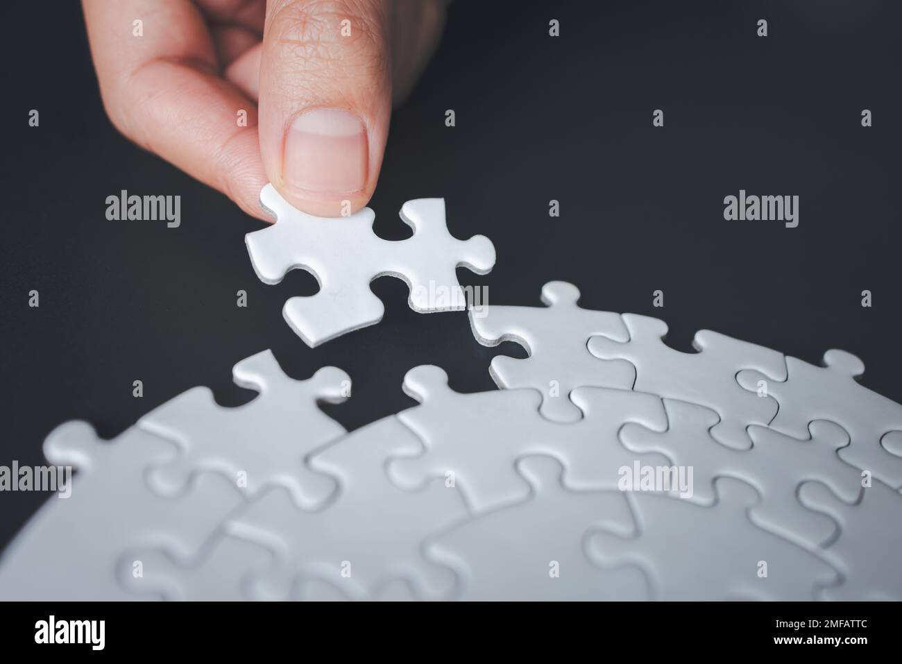 Hand put last piece of jigsaw puzzle. White unfinished jigsaw puzzle ...