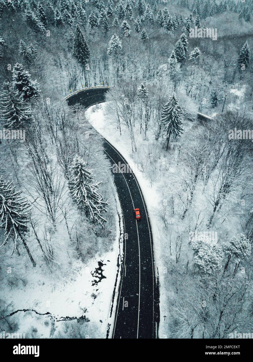 Aerial view of a red car traversing winding road in winte forest ...