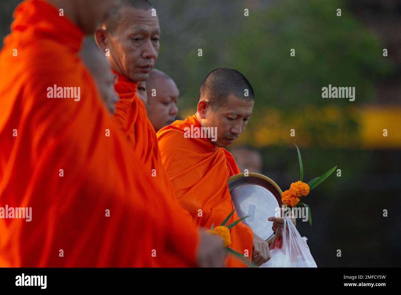 Monks adorned in bright orange robes standing in a line performing ...