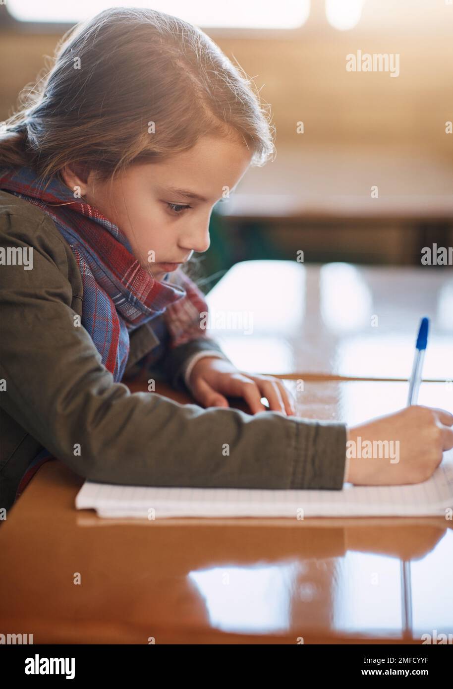 Focused on her work. an elementary school girl doing her school work in ...