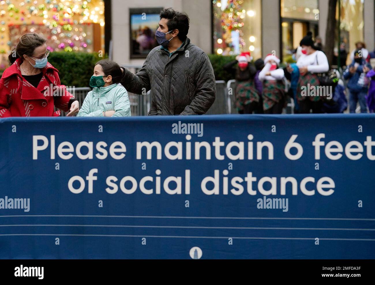 A family walks behind a sign reminding people to keep their distance as ...