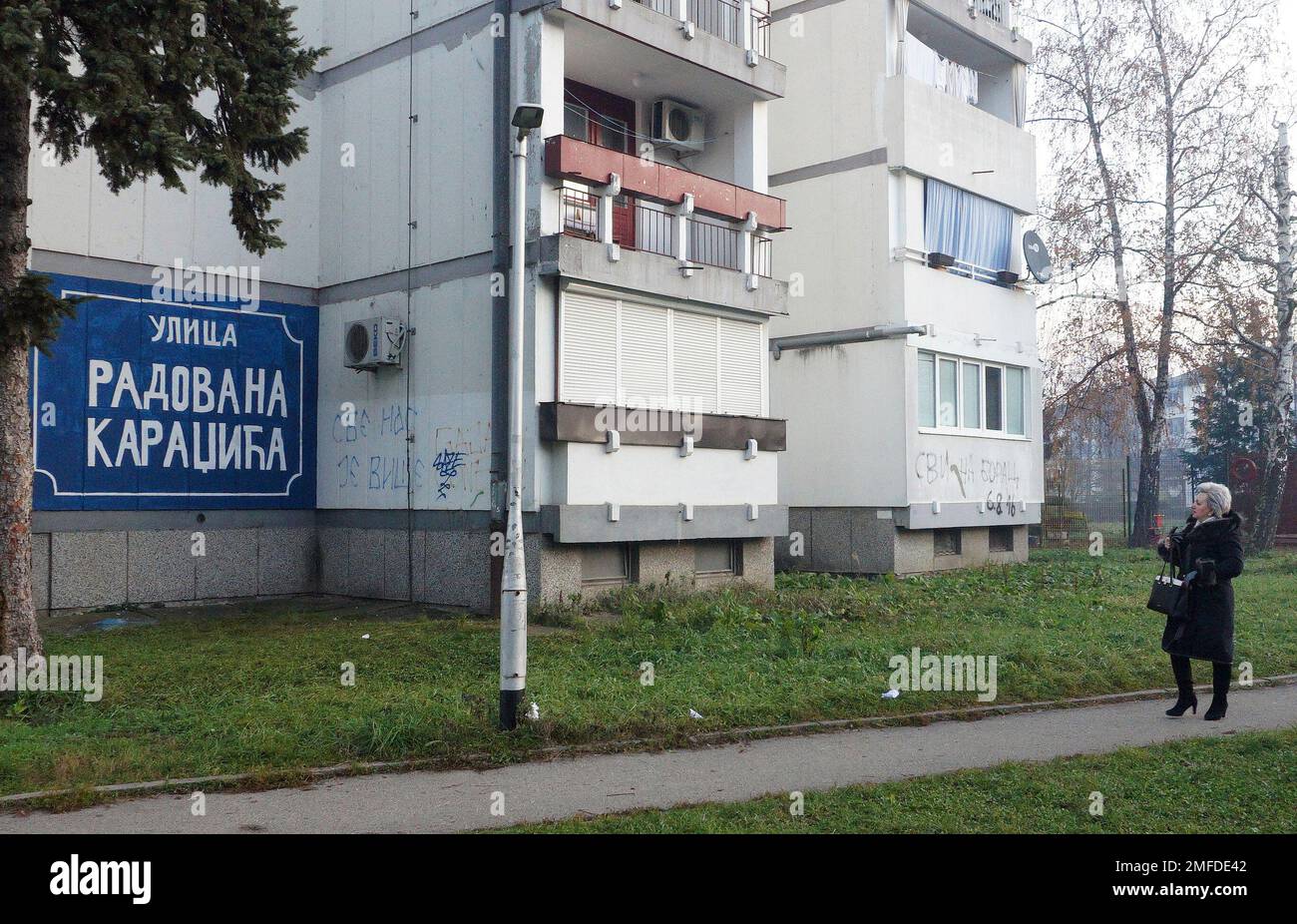 A woman walks past a graffiti on a wall showing the street sign reading ...