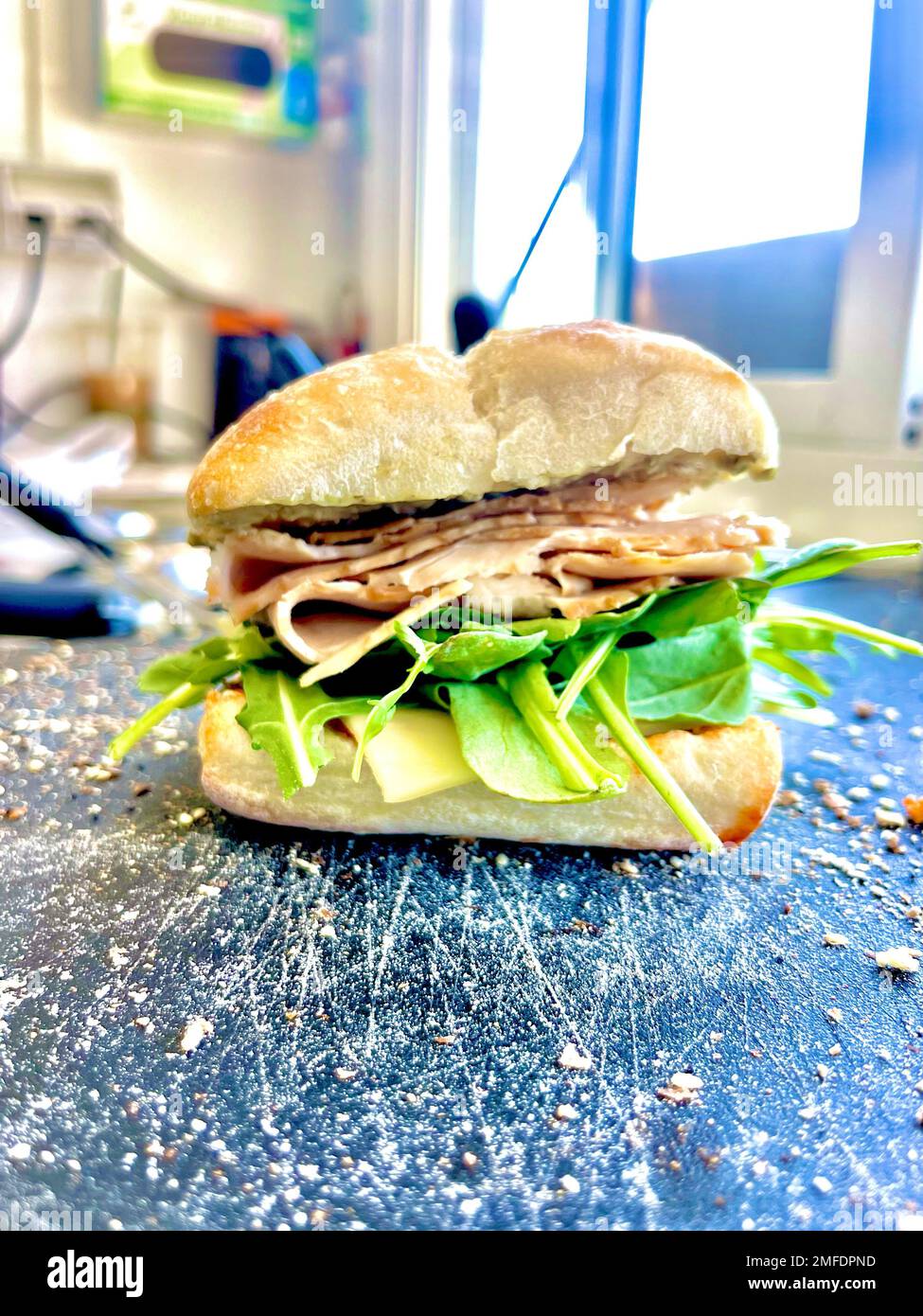 A vertical closeup of a sandwich with ham and greens in the kitchen ...