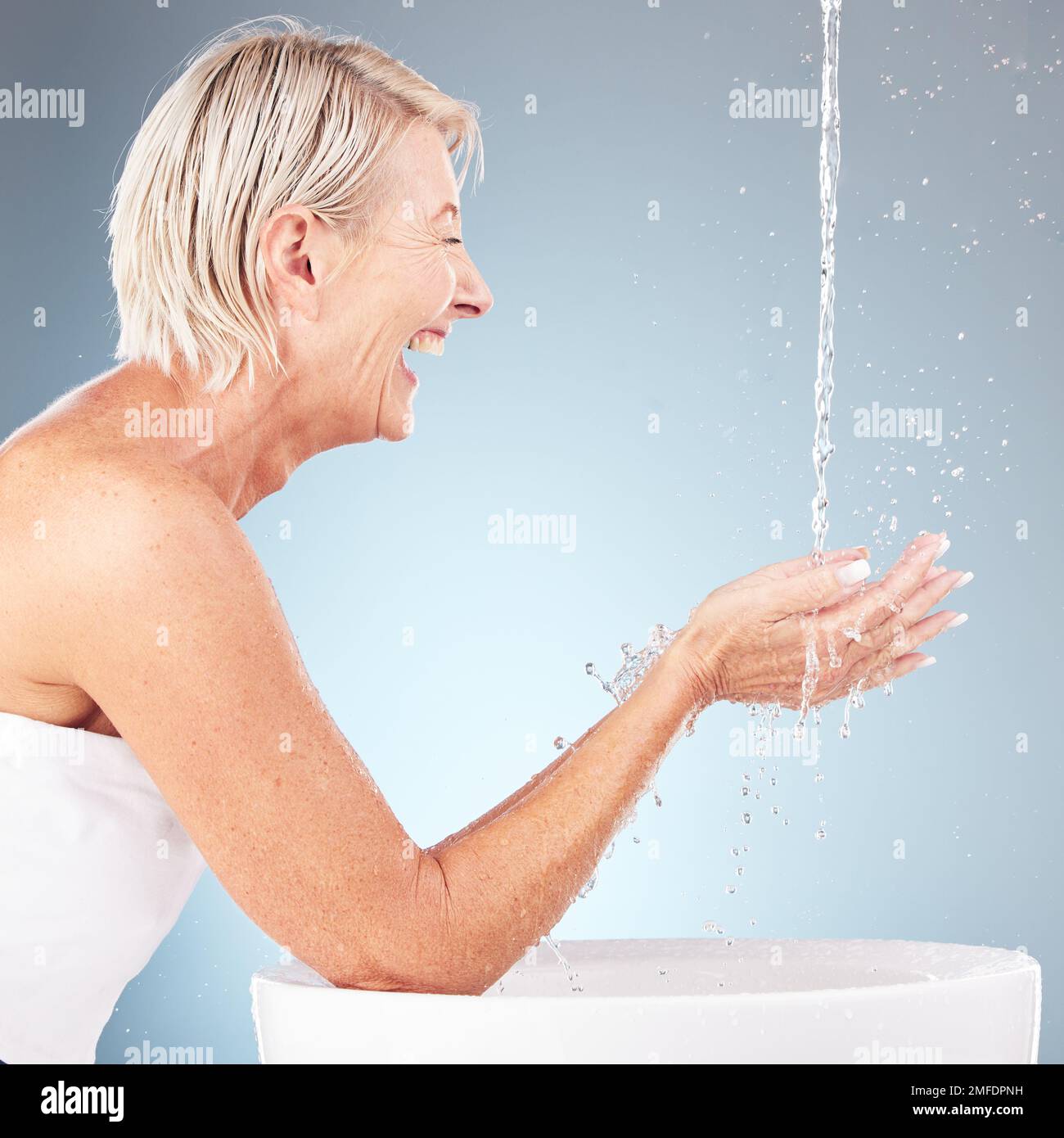 Senior woman, water splash and washing hands for wellness, beauty and skincare health on studio ...